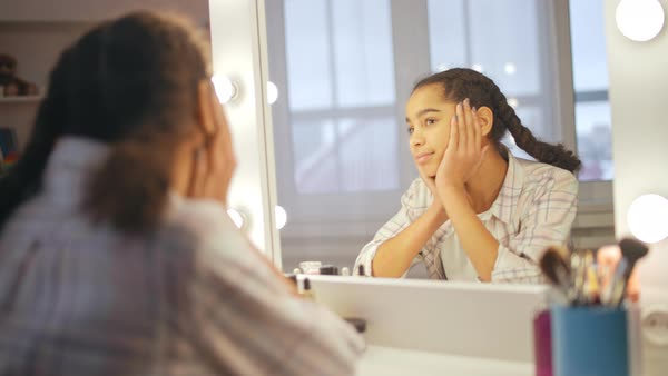 Cute teenage girl looking at her reflection in mirror, happy with her ...