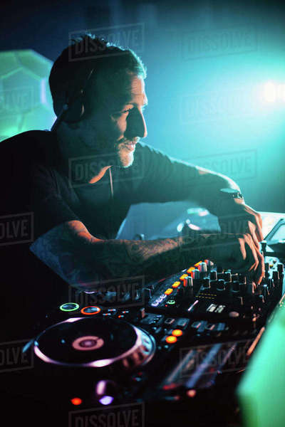 Profile shot of a young Caucasian male DJ playing the track in a blue ...