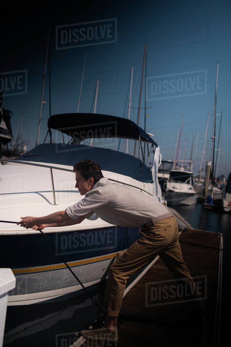 Side view of young man holding rope while standing on wooden pier with ...