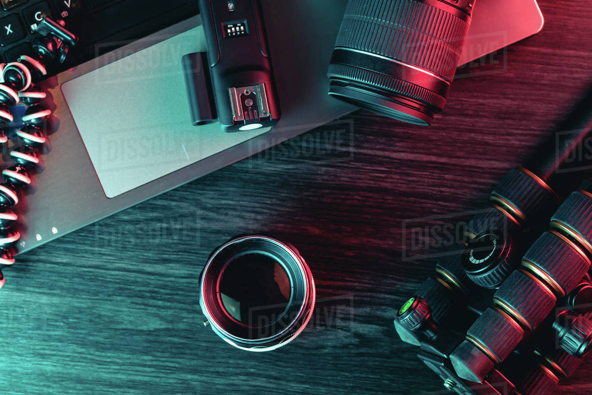 A desk working with a laptop keyboard, modern camera, lens, tripod, and ...
