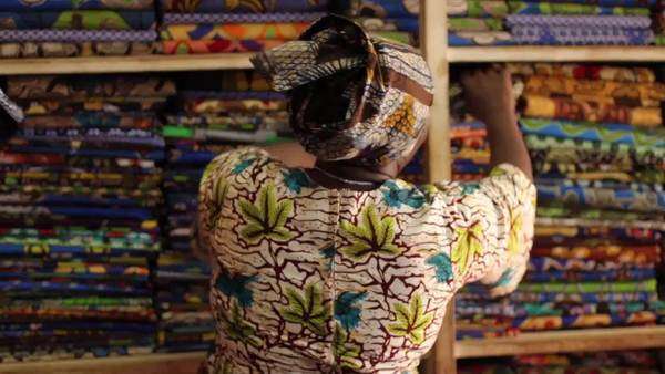 African lady in traditional clothing in fabric shop looking at fabric ...
