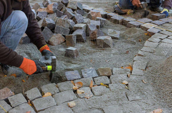 Construction worker laying granite cubes stone pavement on the road of ...