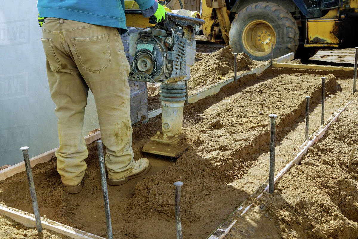 Worker compressed sand in around new sidewalk with special working tool ...
