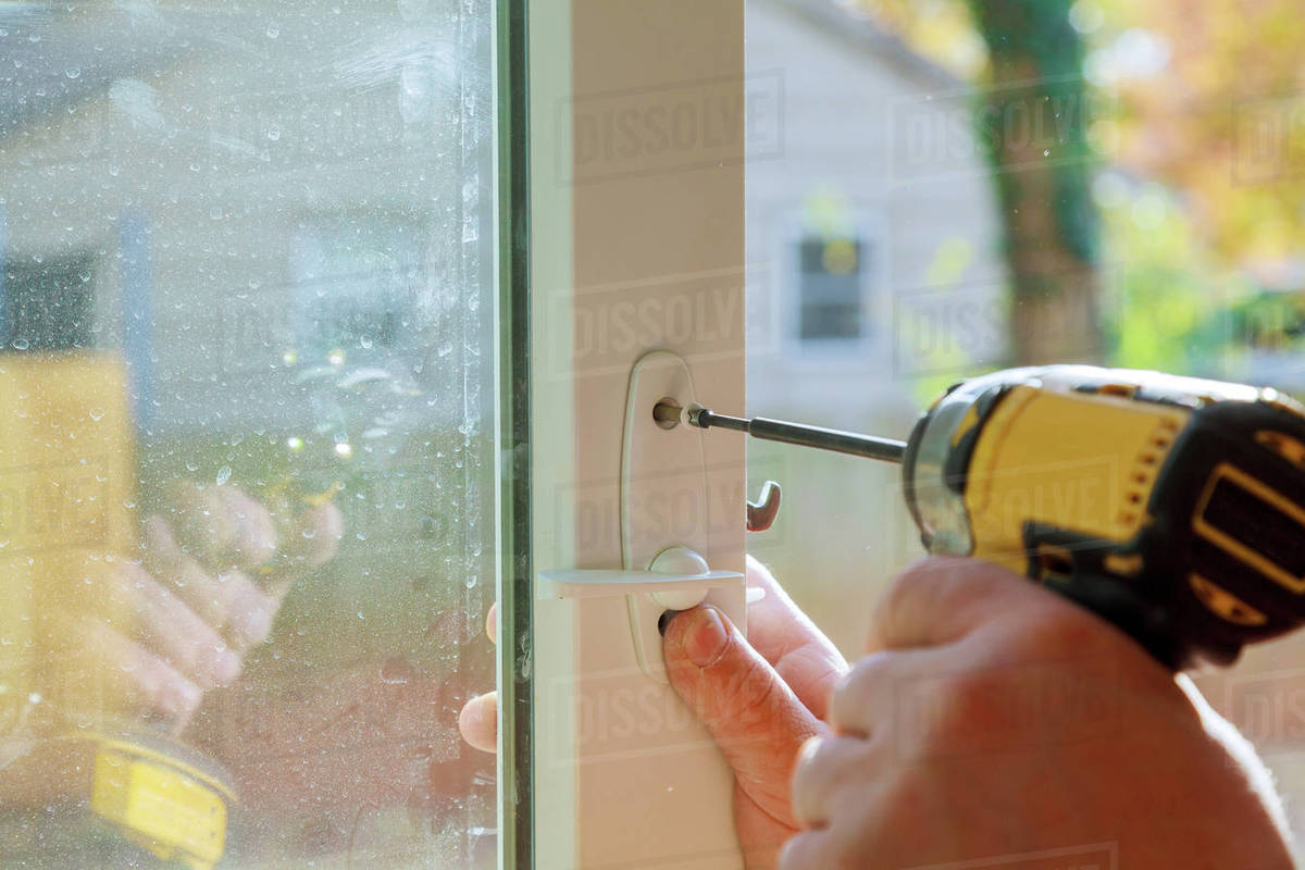 Handyman using a screwdriver drill to installing lock in door in a ...