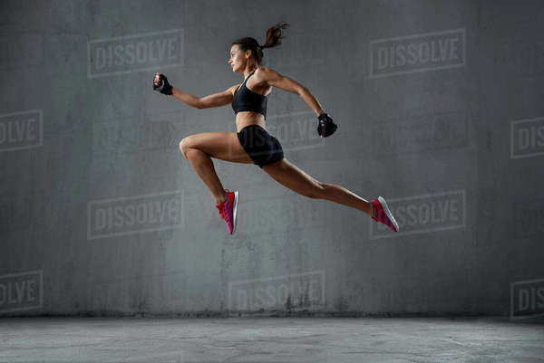Isolated portrait of athletic woman jumping in hall, loft gray interior ...