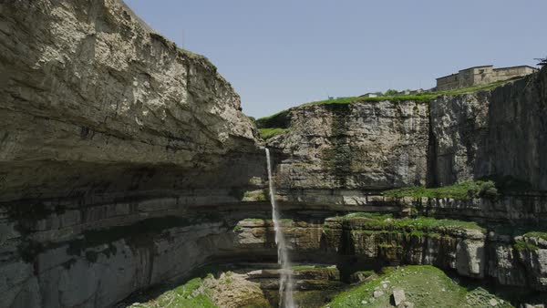 Narrow waterfall falls from high cliff. Action. Top view of water from ...