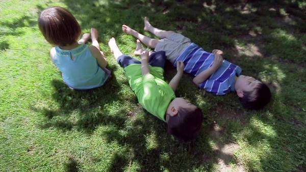 Three children relax in the shade of a tree on a hot summer day (slow ...