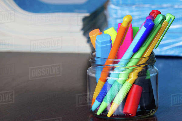Multi-colored pens and markers in a stand on the background of Stack of ...