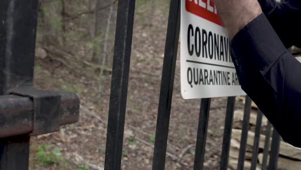 Tilt up of a man putting up a Keep Out Coronavirus Quarantine Area sign ...