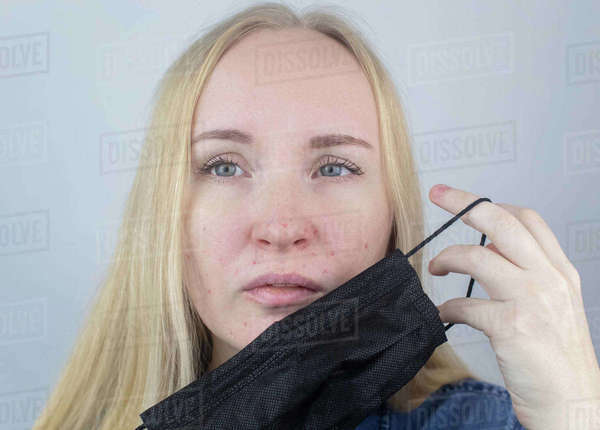 Woman removes the protective mask and shows irritation on face skin ...