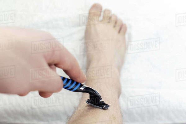 A man on a white background shaves his legs. Hairy legs and care ...