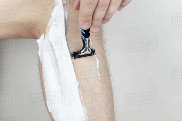 A man on a white background shaves his legs. Hairy legs and care ...