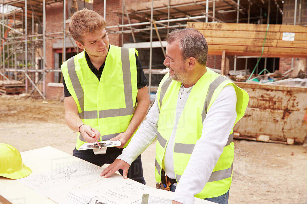 Builder on building site discussing work with apprentice - Royalty-free ...