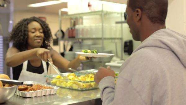 Volunteers in kitchen of homeless shelter serves food to people ...