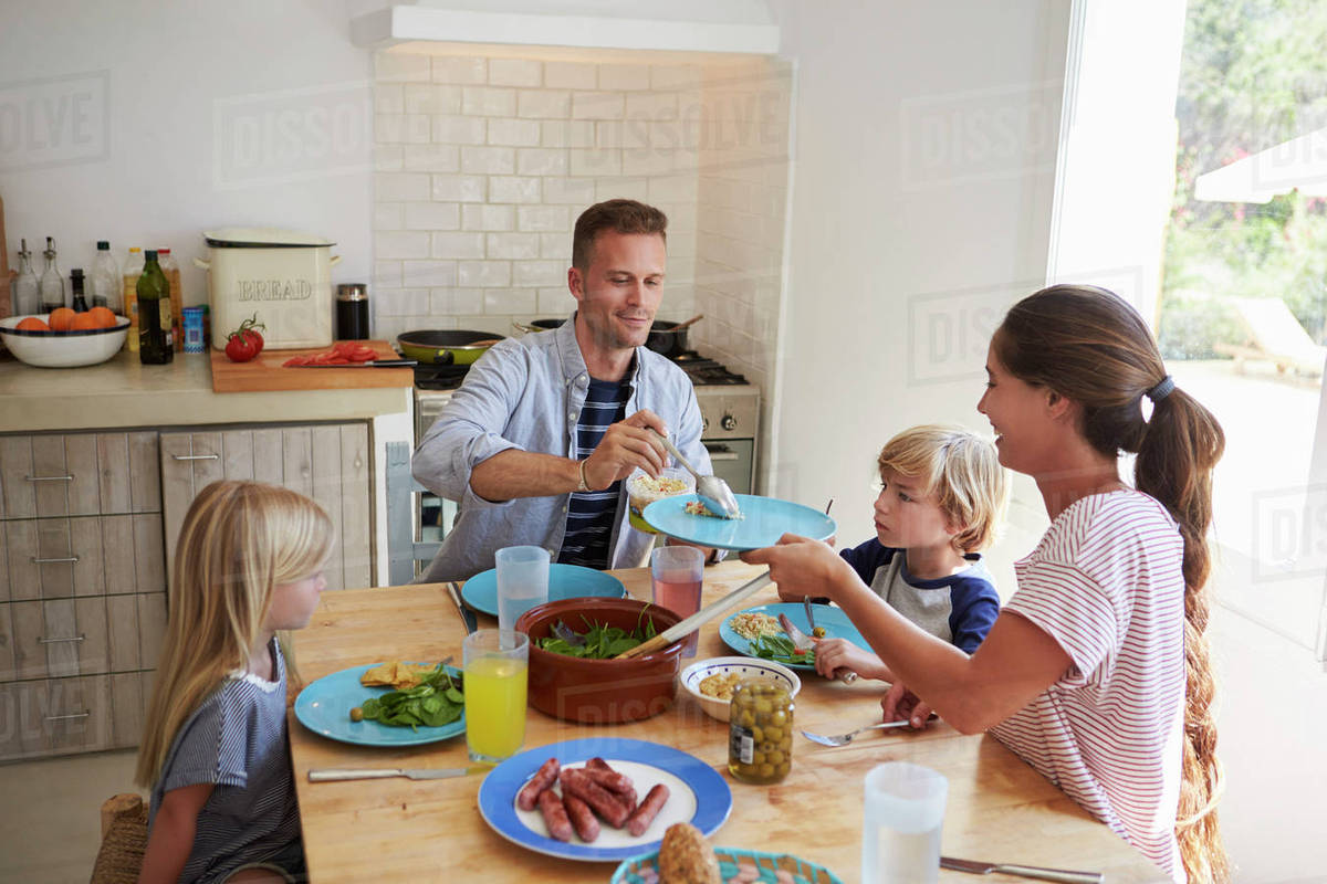Family sitting around kitchen table serving lunch - Royalty-free Stock ...