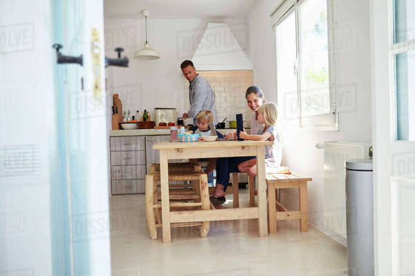 Kids at kitchen table with mum, dad cooks, view from doorway - Stock ...