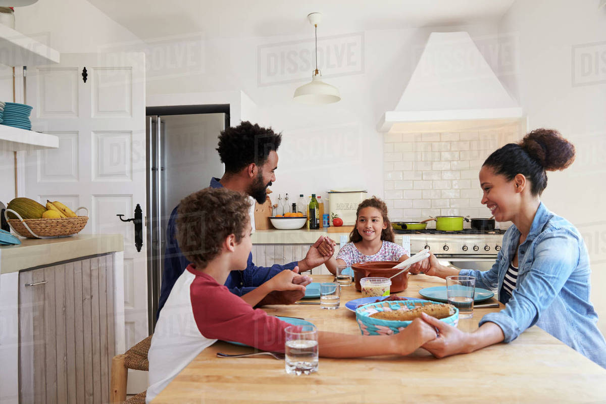 Family hold hands around the kitchen table before their meal - Stock ...