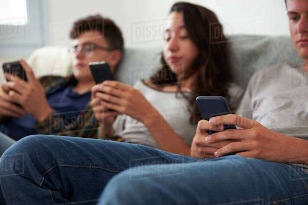 Three teenagers sitting together using smartphones at home - Royalty ...