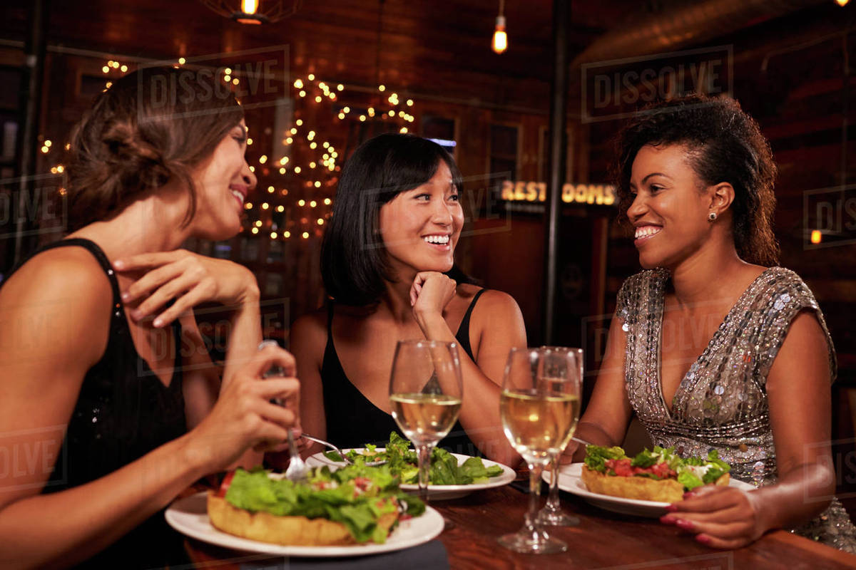 Three female friends eating dinner together at a restaurant - Royalty ...