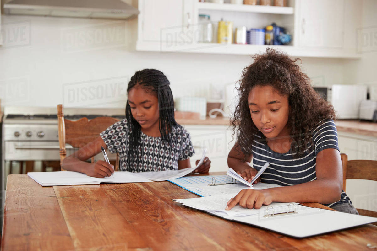 Two Sisters Sitting At Table In Kitchen Doing Homework - Royalty-free ...
