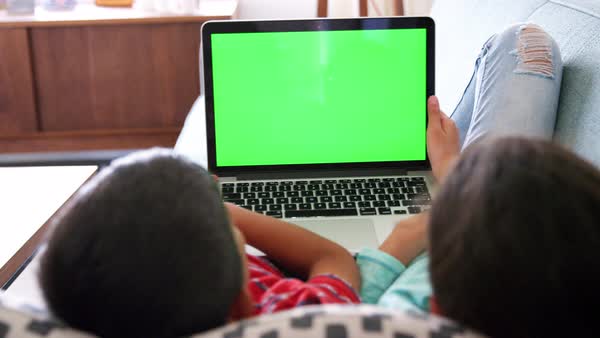 Rear View Of Brother And Sister Lying On Sofa At Home Using Laptop ...