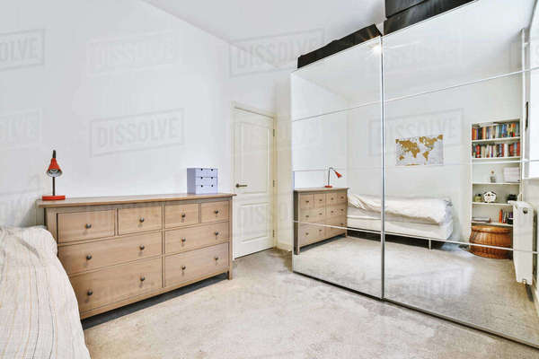 Simple single bedroom with chest of drawers and mirror wardrobe against ...