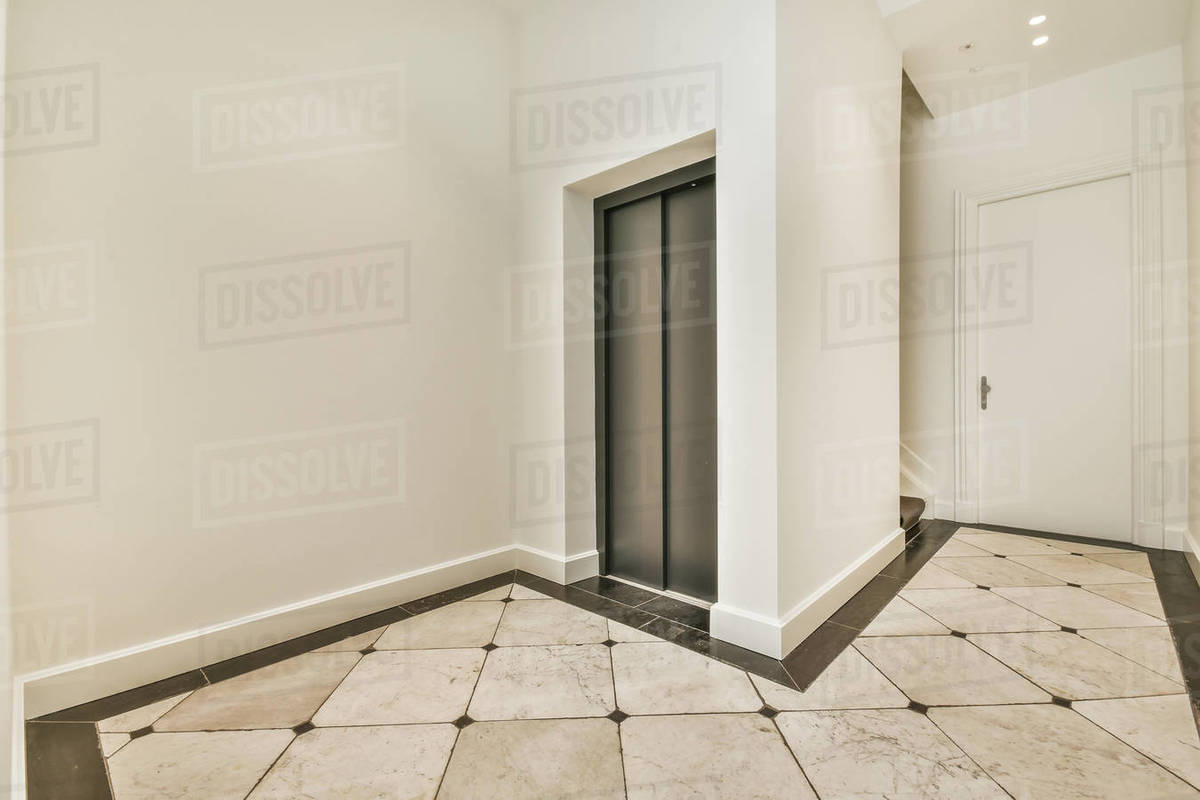 Interior of spacious hallway with metal elevator and tiled floor in ...