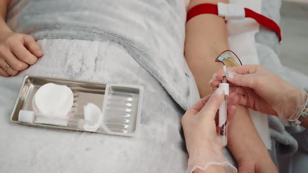 Nurse taking a blood sample from a patient lying in a hospital ward ...