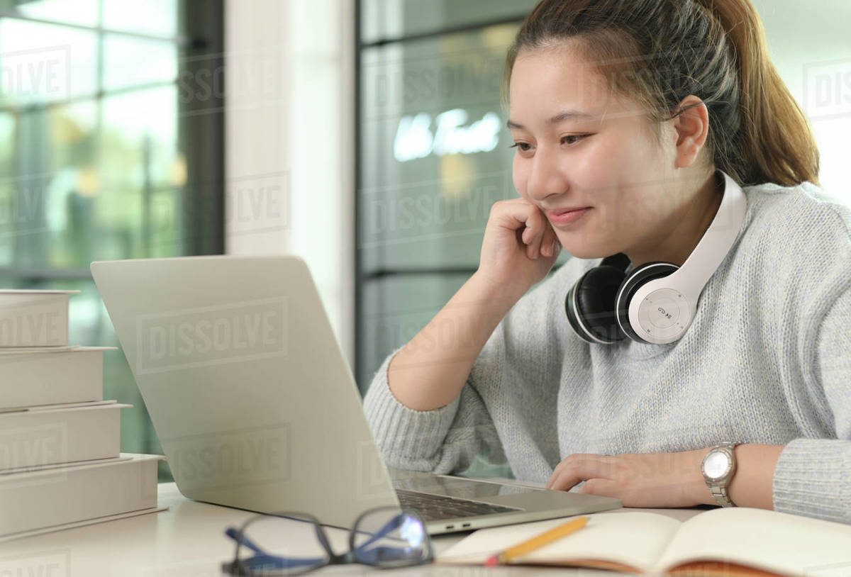 Teenage girl sitting looking at the laptop screen and smiling, wearing ...