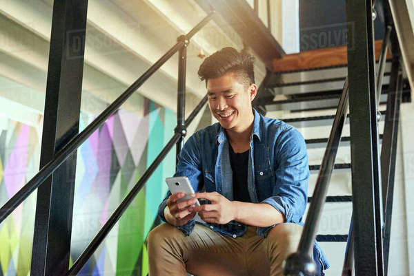 Asian man, texting and office stairs with smartphone, smile and ...