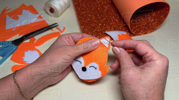 Woman sews toy fox ear to its muzzle, creating felt toy. Hands of ...
