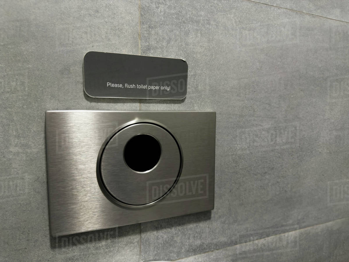 Button on wall to flush toilet. Warning sign in public toilet. Only ...