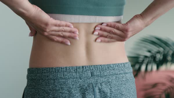 Woman massages low back muscles with both hands as camera wraps around ...
