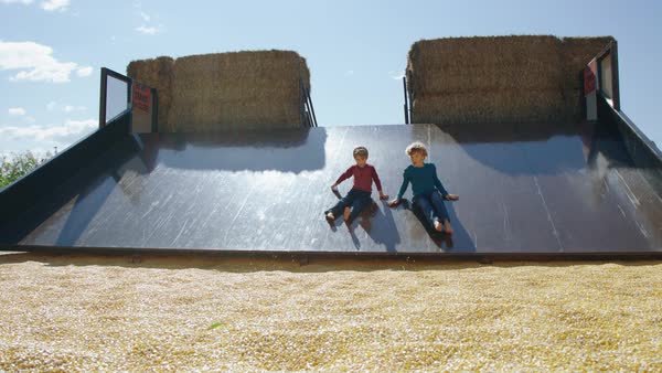 Two boys slide into huge pile of hardened corn kernels in slow motion ...
