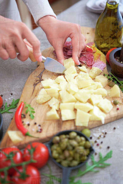 Woman chopping Parmesan cheese with knife on grey table at domestic ...