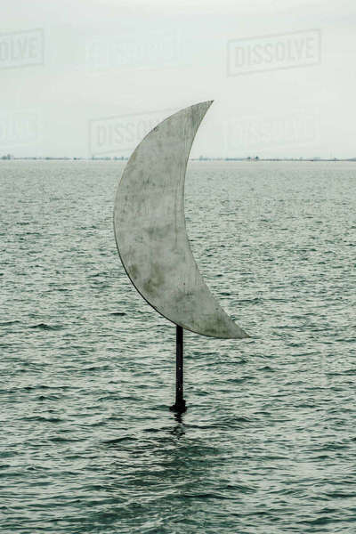 Day view of moon artwork installation above a calm sea level under hazy ...
