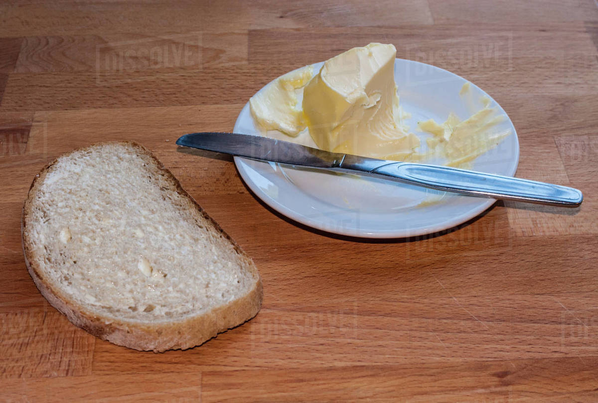 Slice of buttered bread with butter on plate and stainless steel knife ...