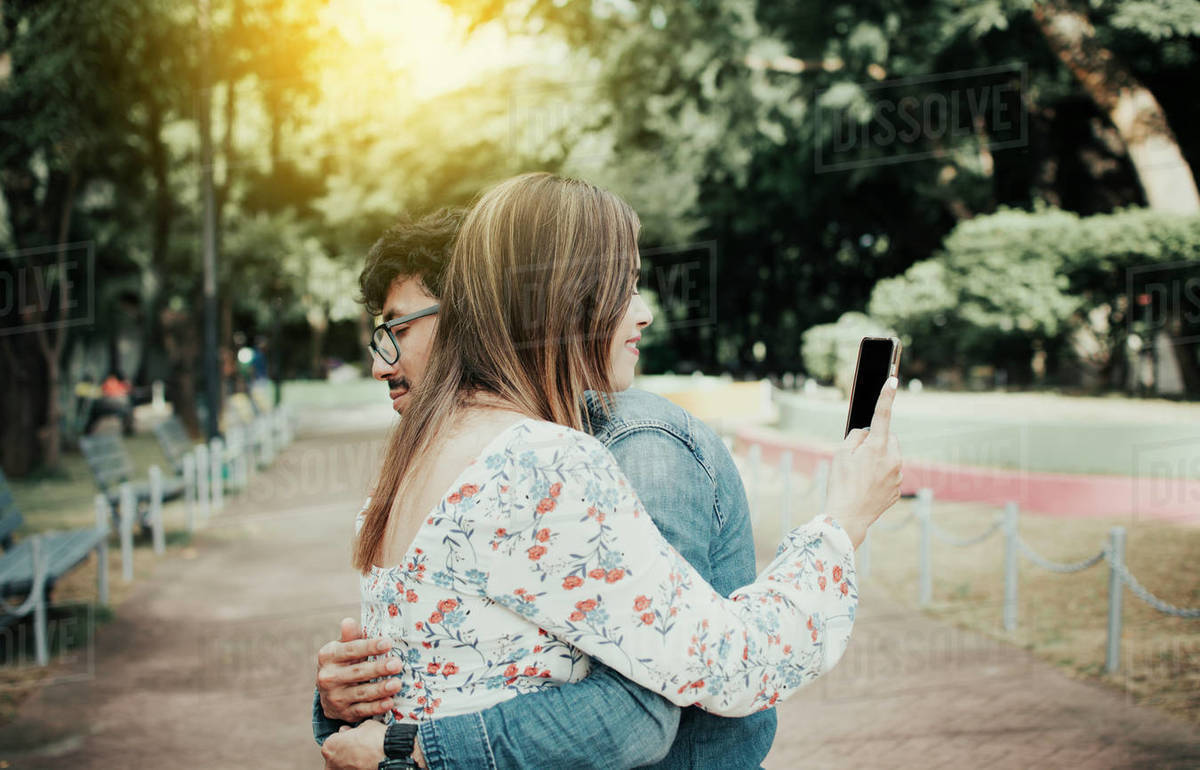 Cheating girlfriend hugging boyfriend and looking at cell phone ...