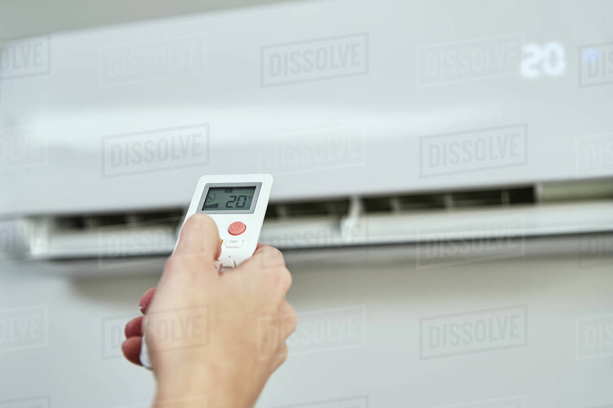 Hand adjusting temperature on air conditioner with remote control ...