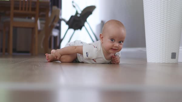 Beautiful baby lying on floor looking to camera, smiling, showing ...