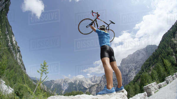 LOW ANGLE: Extreme sportsman standing on ledge lifts his bicycle after ...