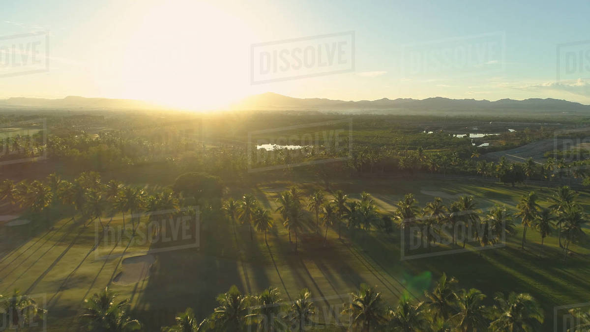 AERIAL, SUN FLARE: Idyllic summer evening sunbeams shine on luxury golf ...