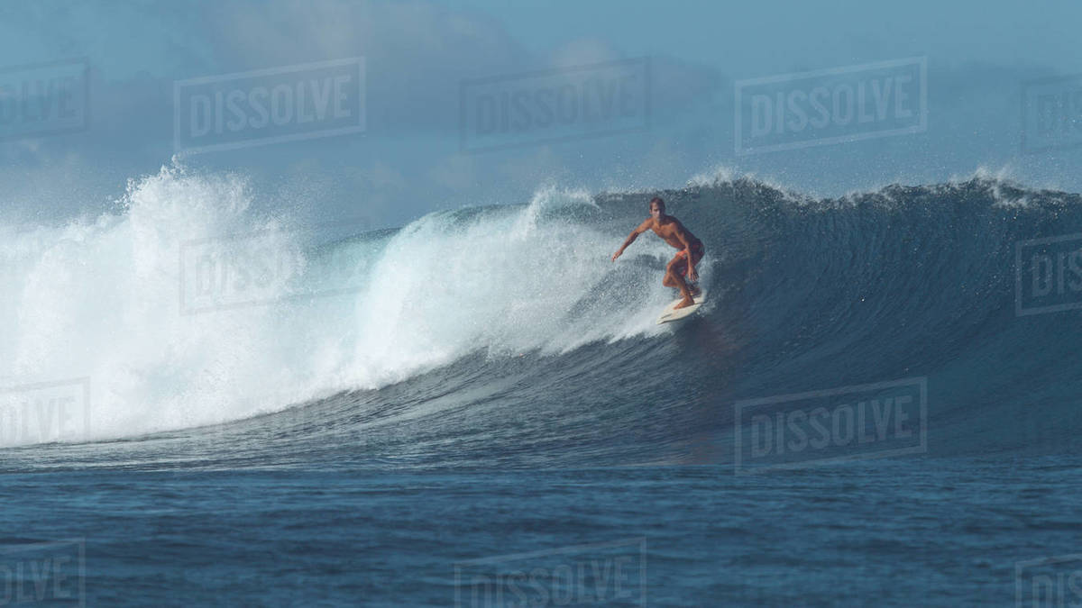Athletic male surfboarder surfs a powerful emerald ocean wave on ...