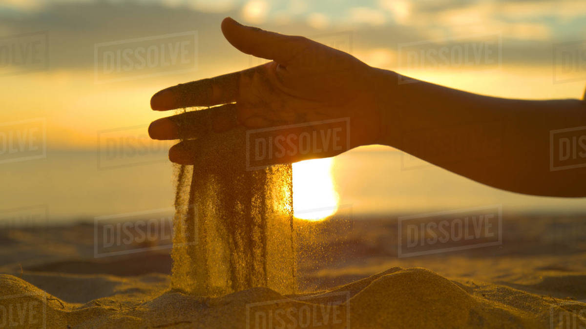 LENS FLARE, CLOSE UP: Sparkling grains of coarse sand fall out of ...