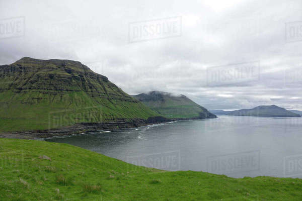 AERIAL: Towering grassy cliff facing the endless blue ocean on a ...