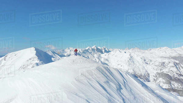 AERIAL: Unrecognizable skier reaches the summit of a snowy mountain in ...
