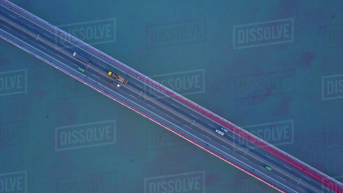 AERIAL, TOP DOWN: Flying above a busy highway bridge crossing the muddy ...