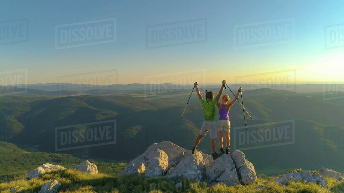 AERIAL, SUN FLARE: Excited Caucasian hiker couple observes the stunning ...