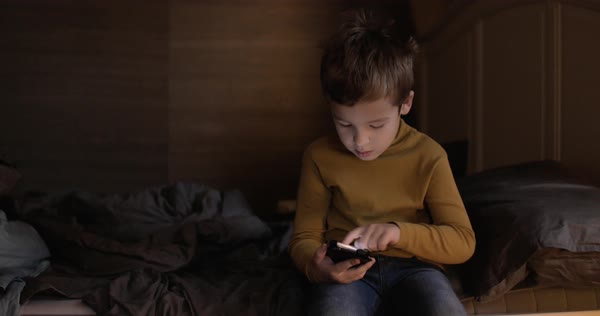 Boy searching for something on mobile. He sitting on the bed with cell ...
