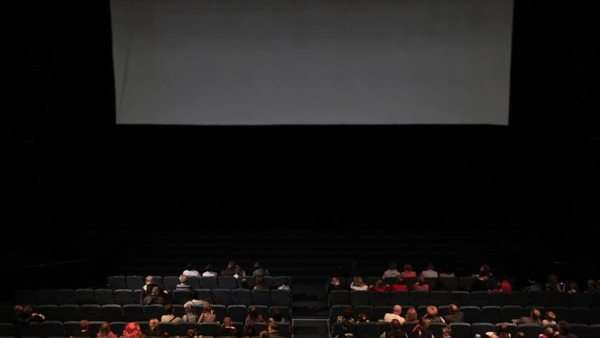Back view of audience in dark cinema hall in front of big blank screen ...